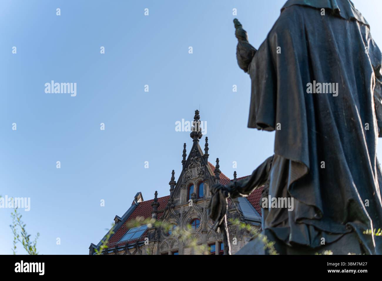 A statue in front of a historic building with ornate gables and a red ...