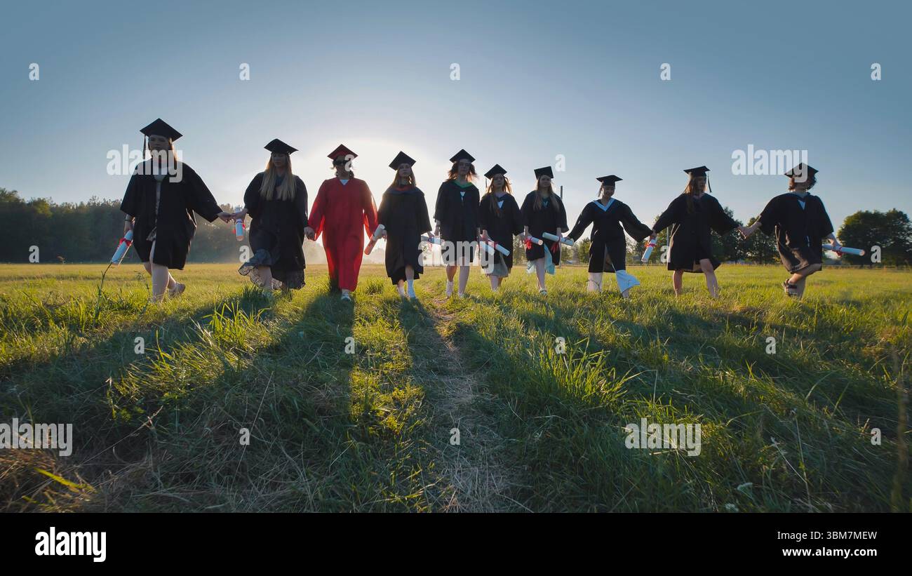 Group of students in graduation gowns walking together with diplomas in ...
