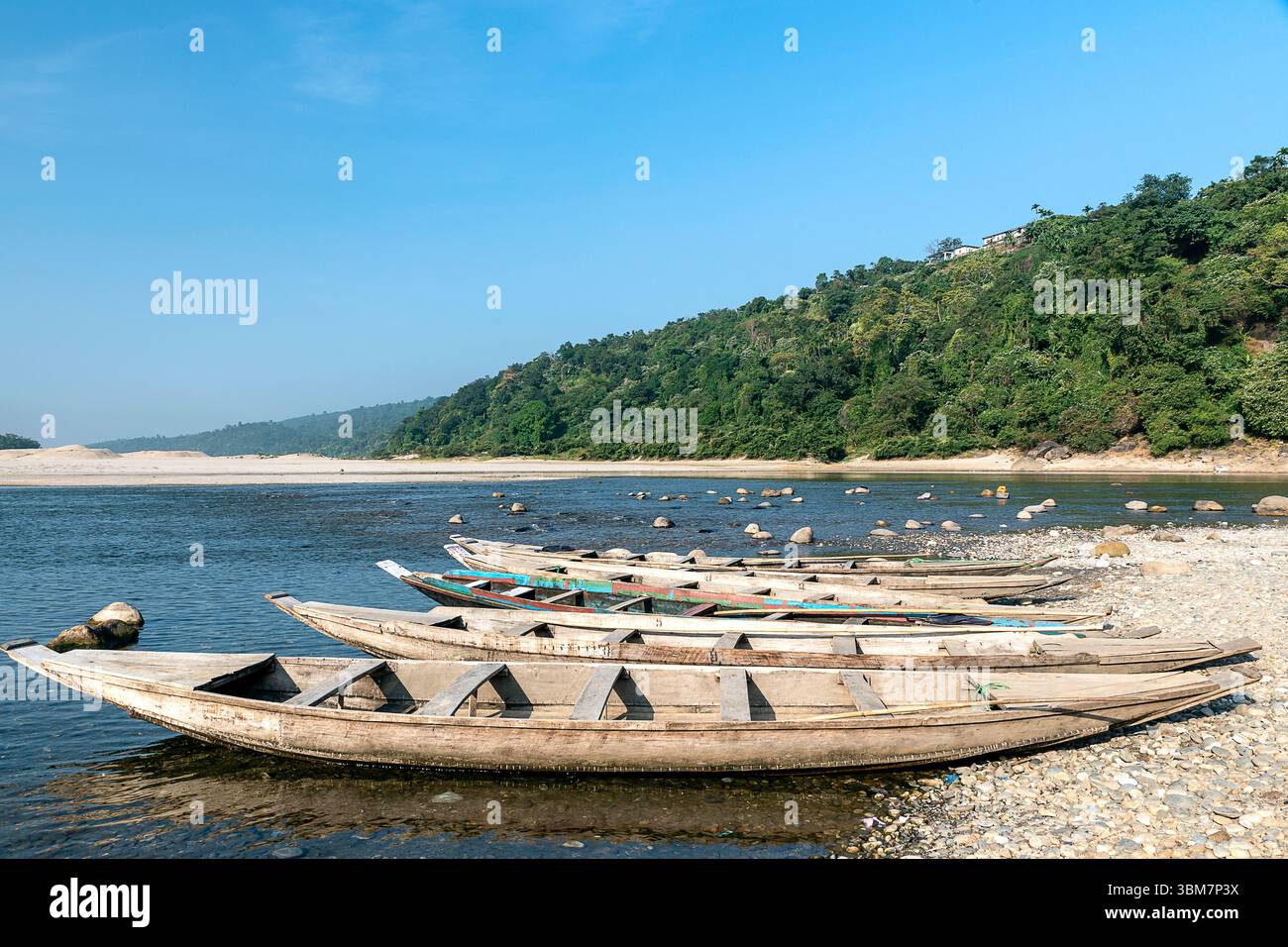 Traditional wooden boats rest along the sandy shore of a calm river ...