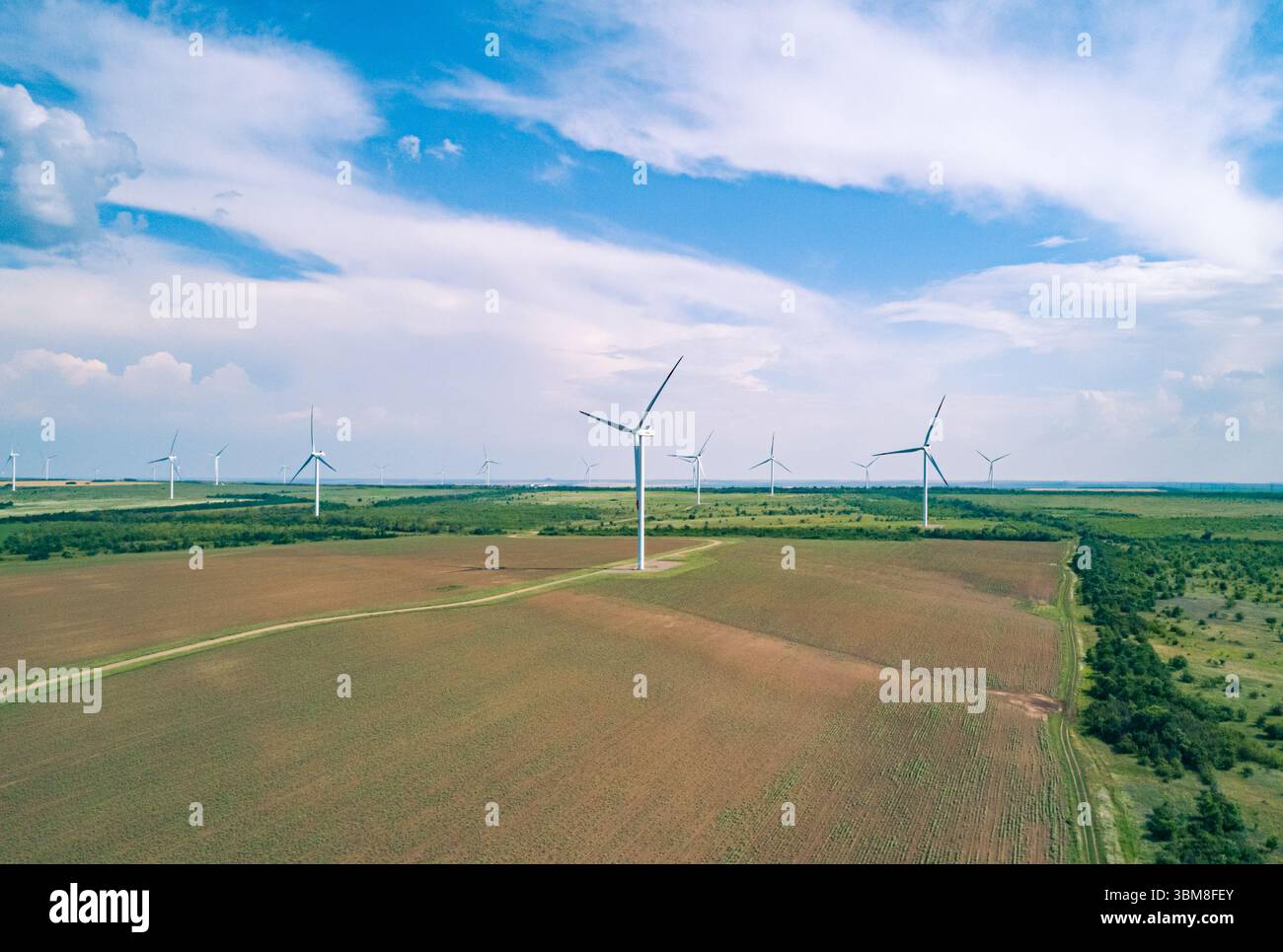 A row of large wind turbines stands tall in a vast, open field ...