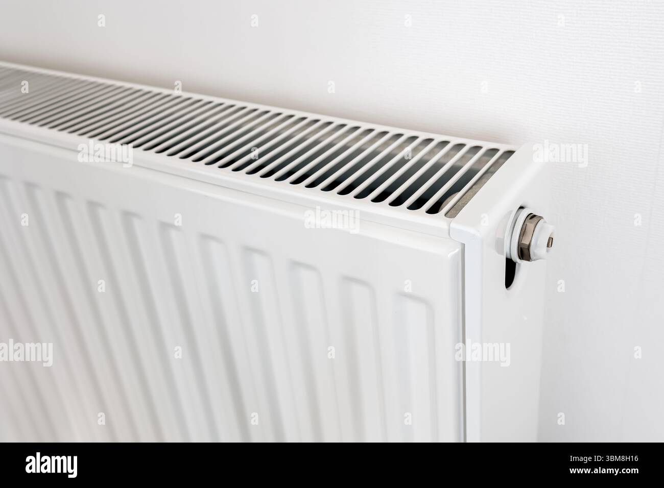 Close-up of a modern white radiator with metal valve and ventilation ...