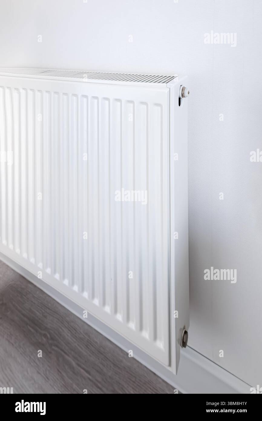Angled view of a white radiator with visible valve and slotted grill ...