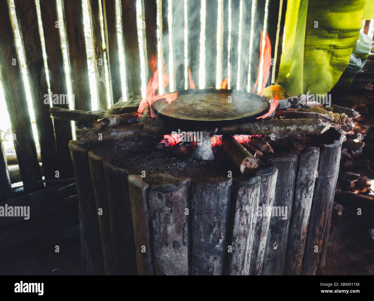 A cassava (yuca) cake is being cooked over an open fire in the ...