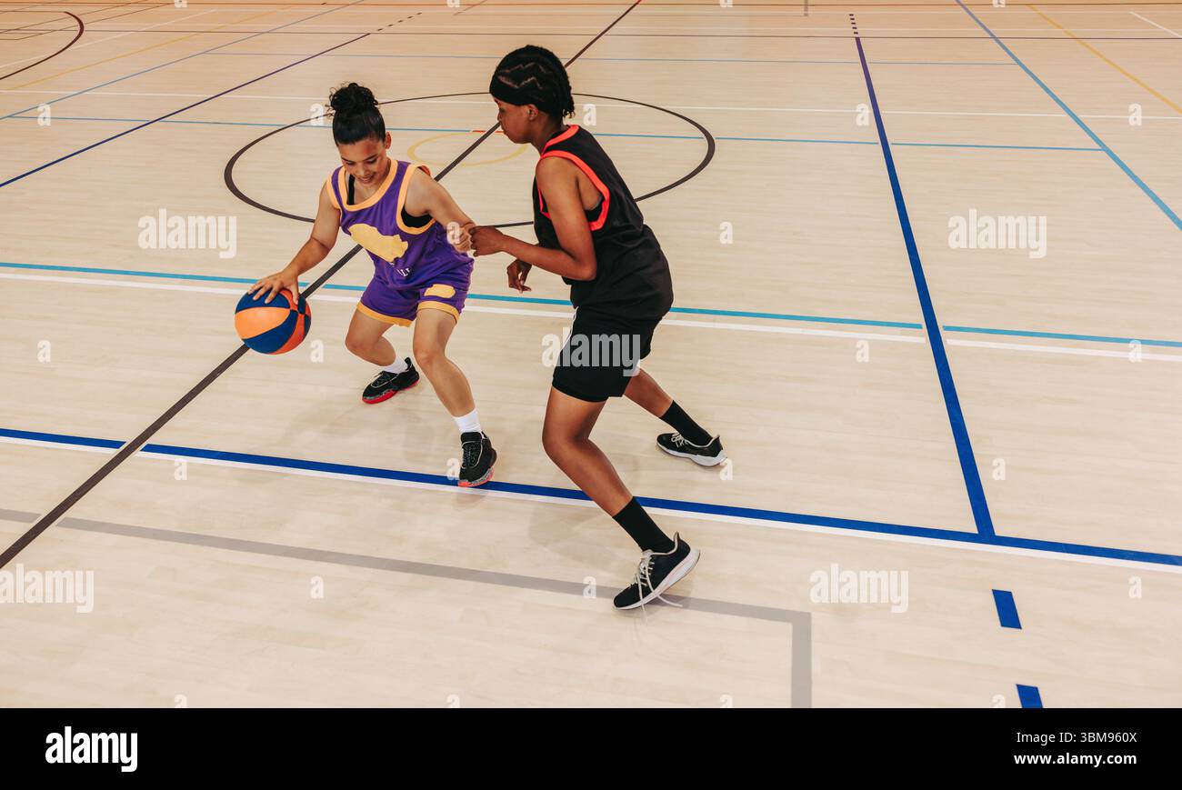 Two young basketball players engage in an intense game on a brightly lit court, showcasing ...