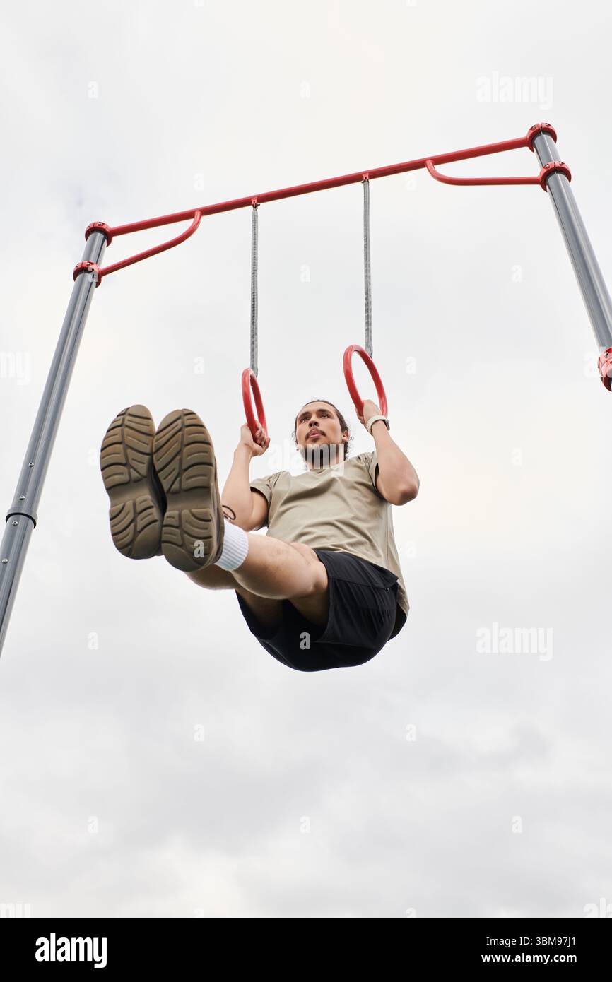 A young sporty man with a beard enjoys a workout on outdoor gym rings ...