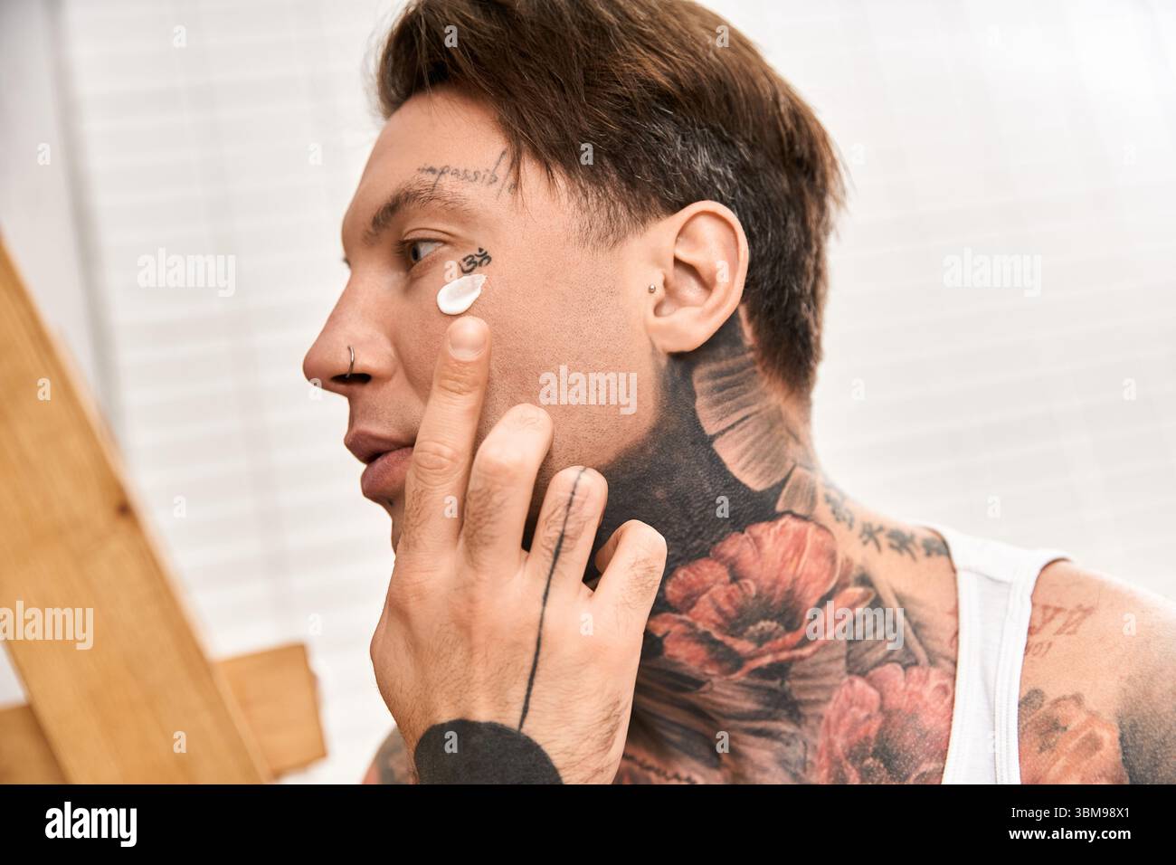 Tattooed man is focused on applying cream to his face, enjoying a laid ...