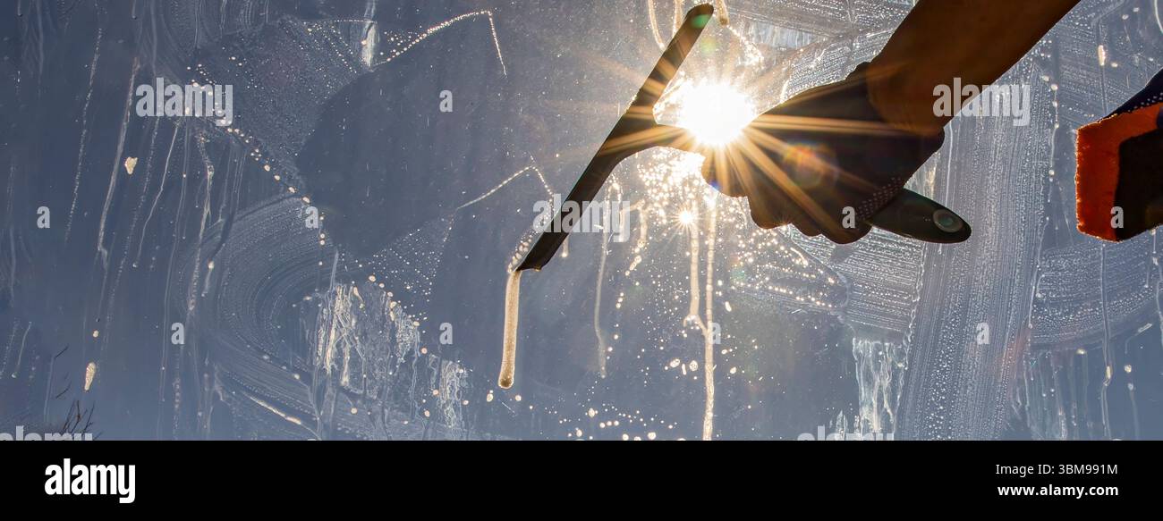 Woman's hand in rubber glove cleaning window with a squeegee on a sunny ...