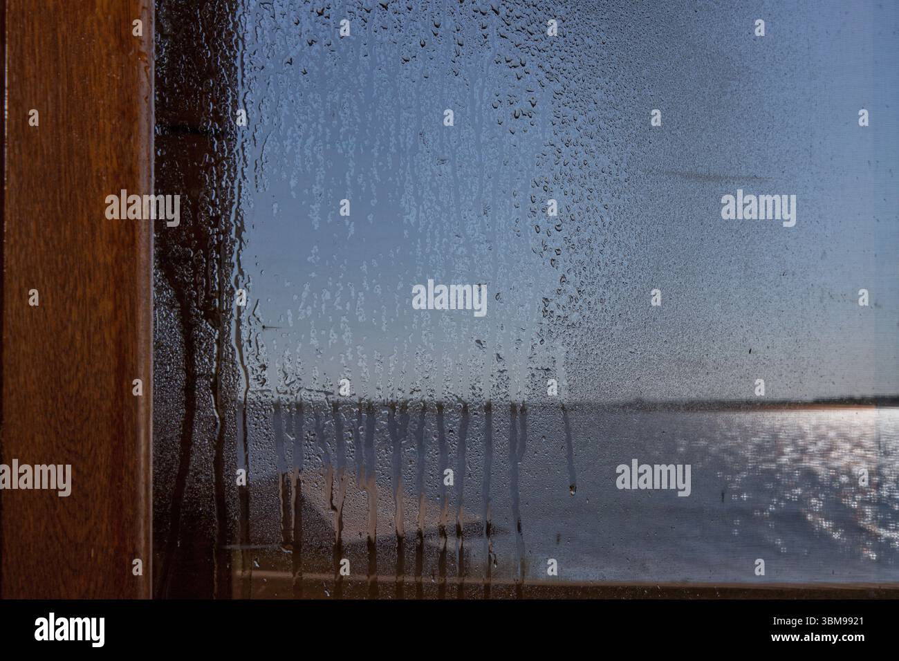 Water droplets and streaks on a glass window with a view of a river and ...