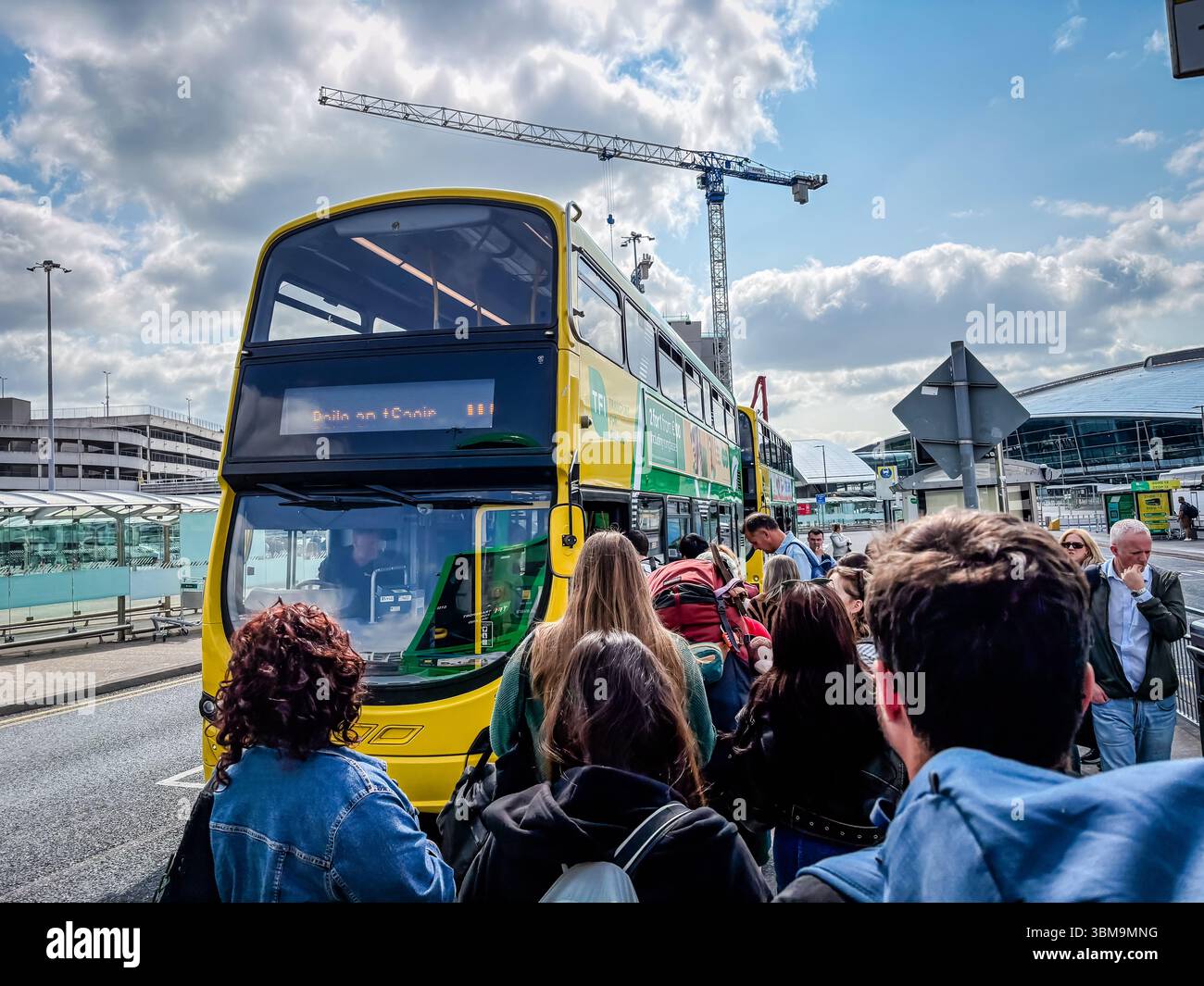 Passengers waiting at a Dublin bus stop as a yellow double-decker bus ...
