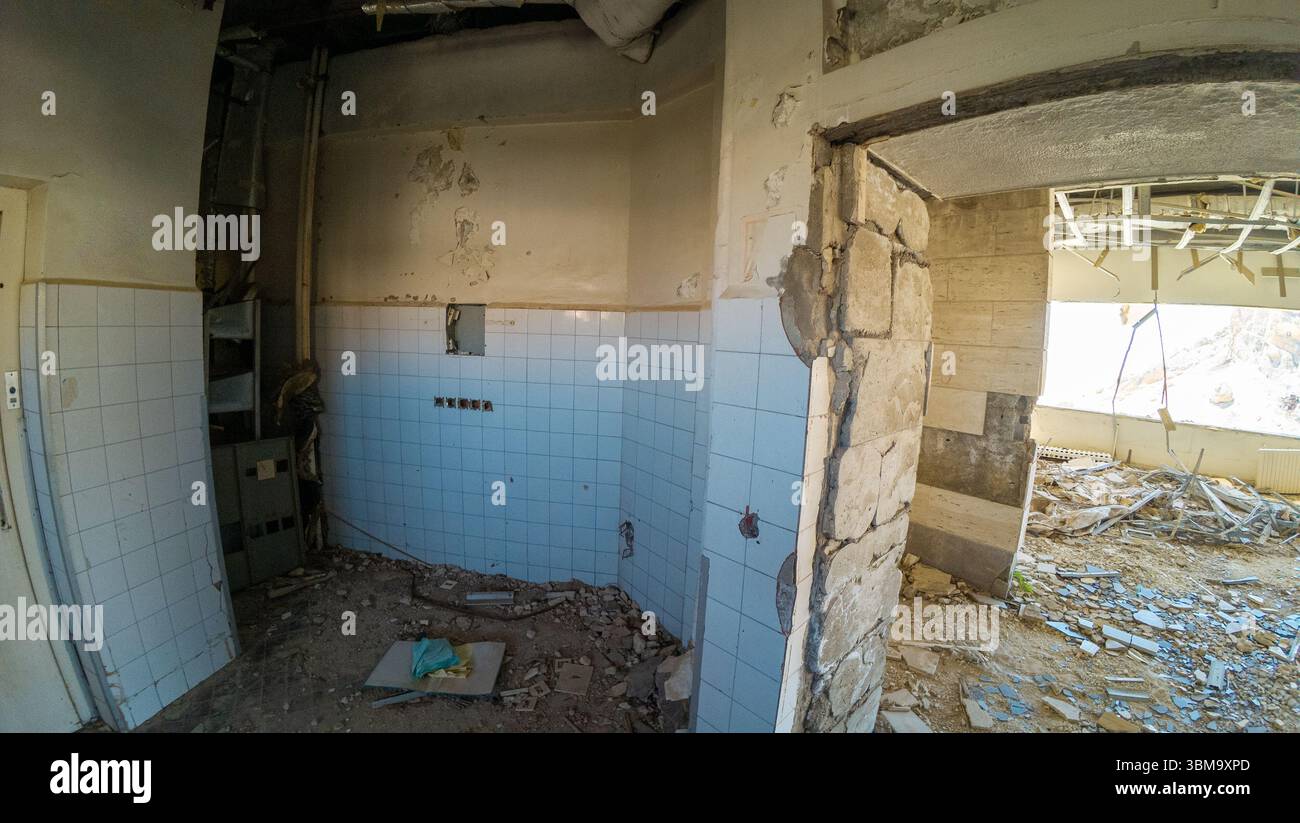 An abandoned room with peeling walls and broken tiles, revealing a dilapidated interior. The ...