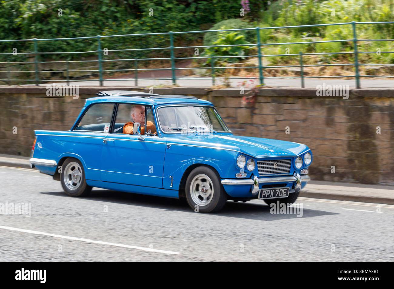 A classic blue Triumph Herald car from the 1960s driving on a city ...