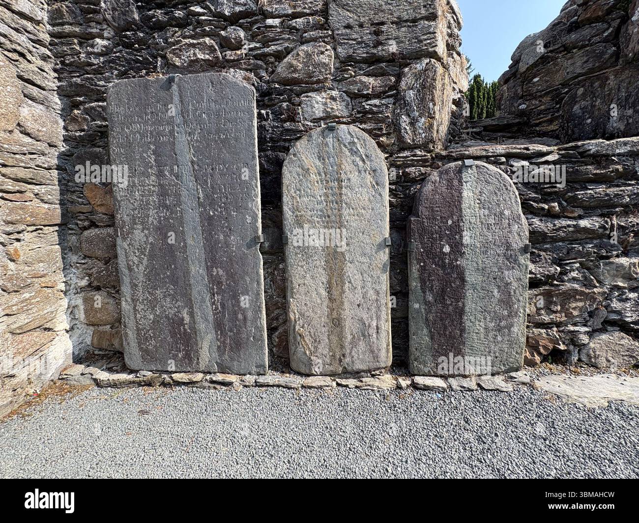 Ancient inscribed stones leaning against a stone wall at Glendalough ...