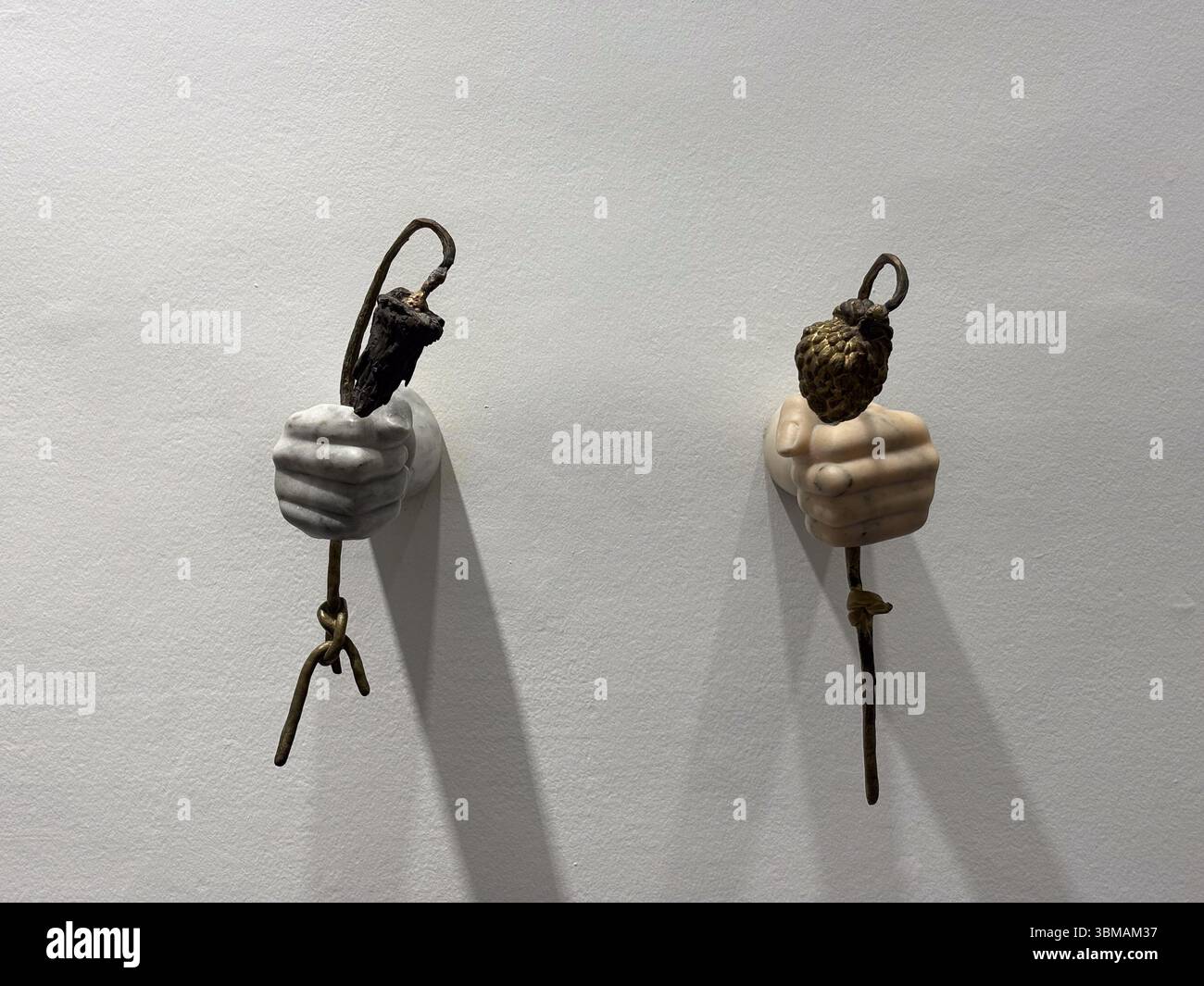 Two small sculptures of hands holding objects are displayed on a white ...