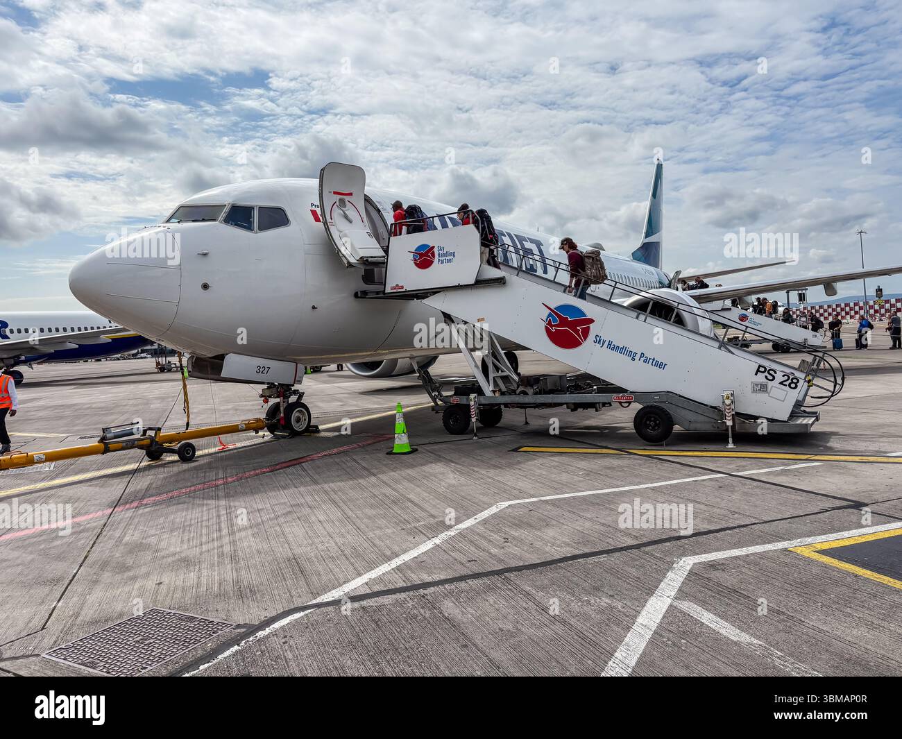 Passengers use mobile stairs to board a jet airplane on the tarmac at ...