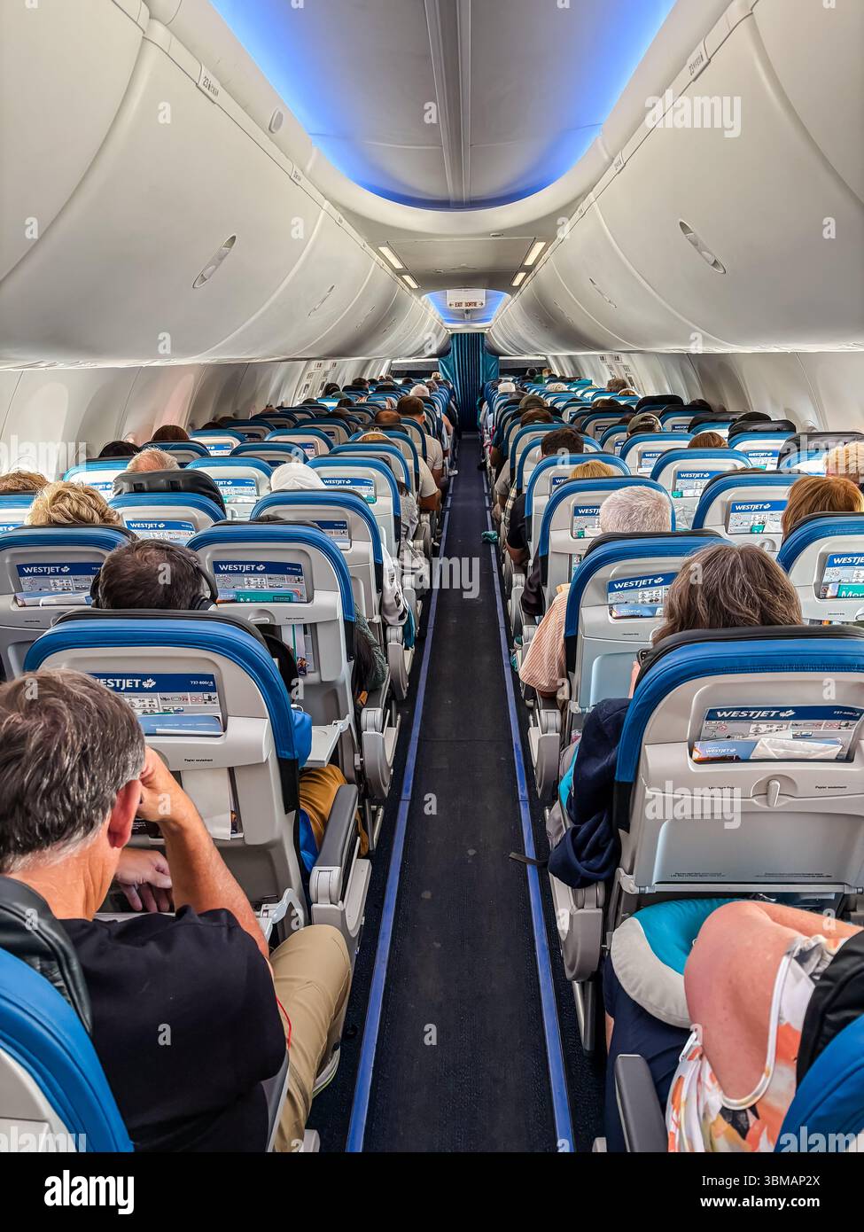 Passengers seated inside a WestJet airplane cabin viewed from the aisle ...