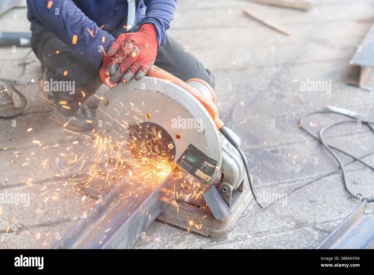 A construction worker operates a cut-off saw, generating sparks while ...