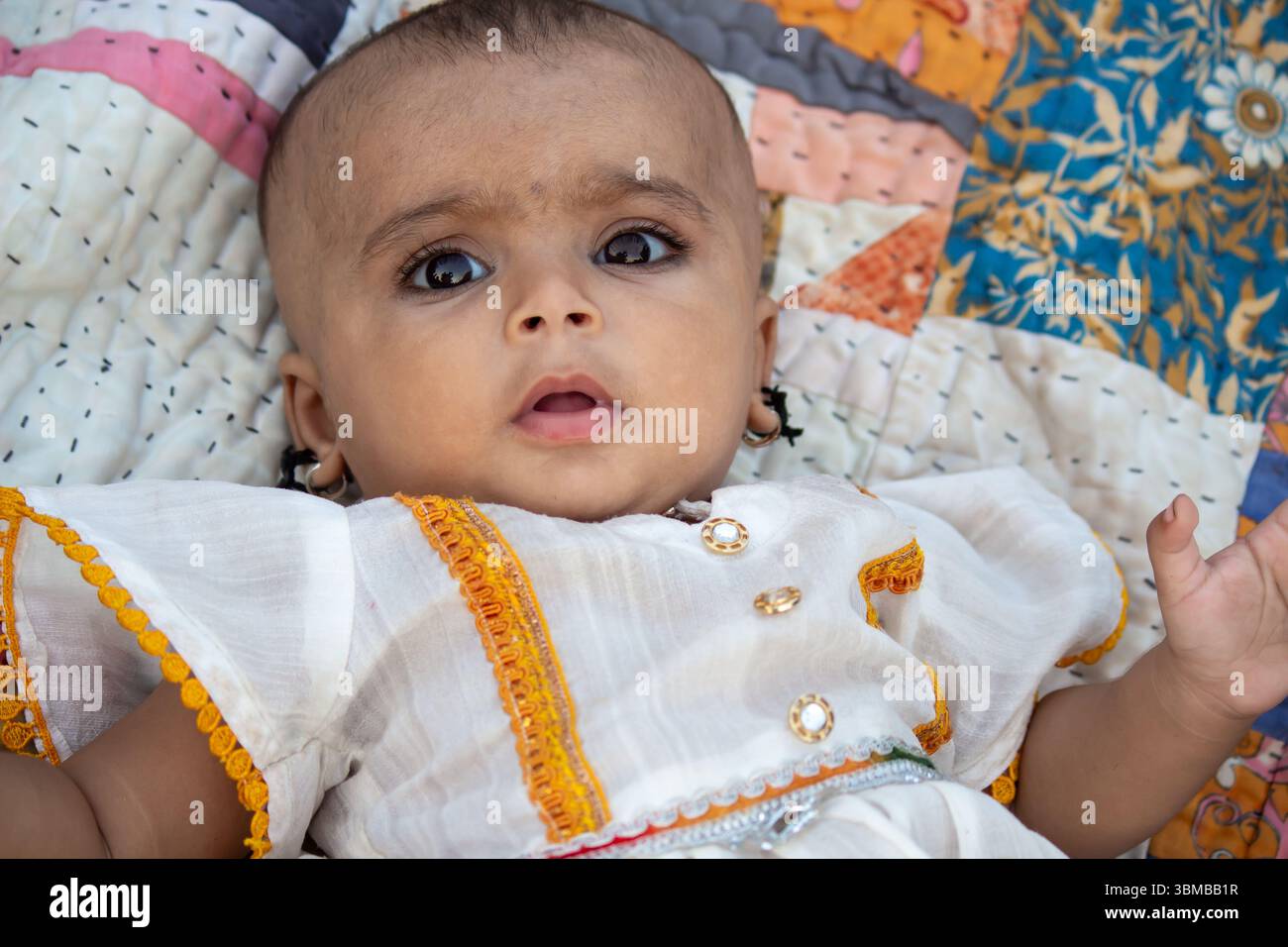 Cute Indian baby in traditional white dress with yellow trim lying on ...