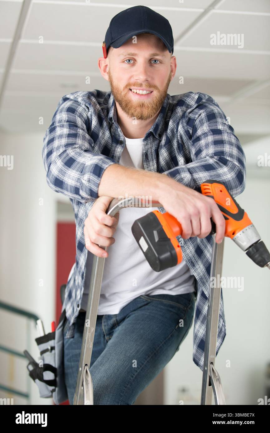 happy male builder standing on ladder with drill Stock Photo - Alamy