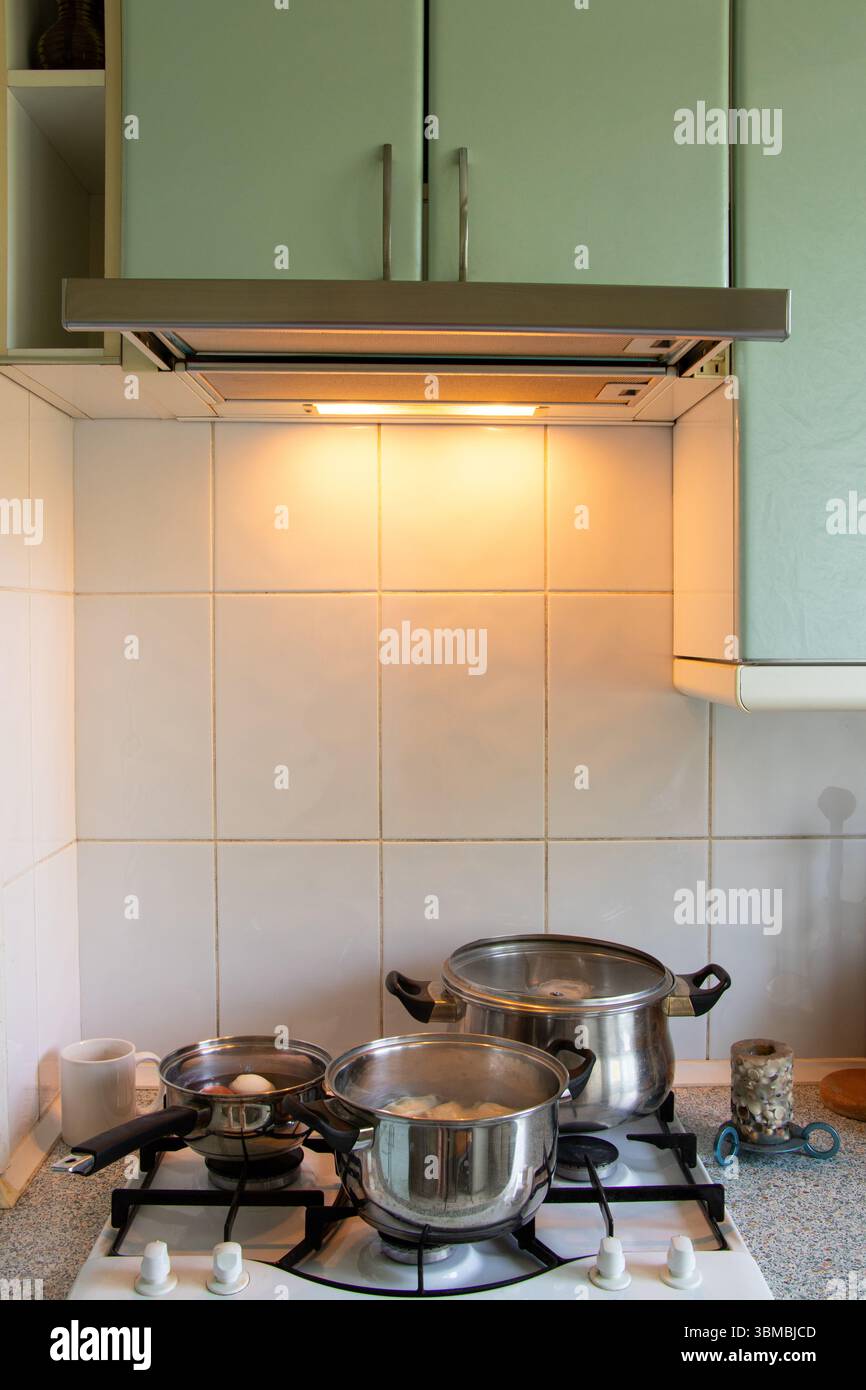 Cooking food in a home kitchen with the hood on and three pots on a gas ...