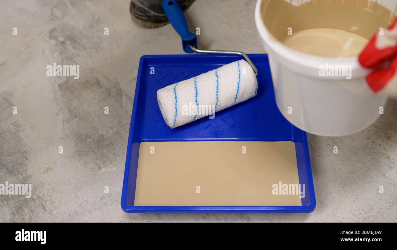 Construction worker pouring beige floor primer into a blue paint tray ...