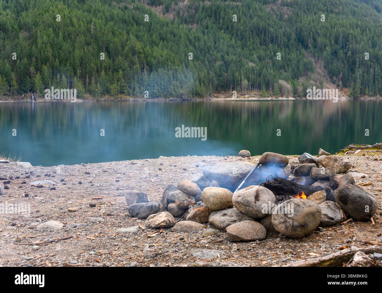A campfire crackles softly on the shore of a peaceful lake, surrounded ...