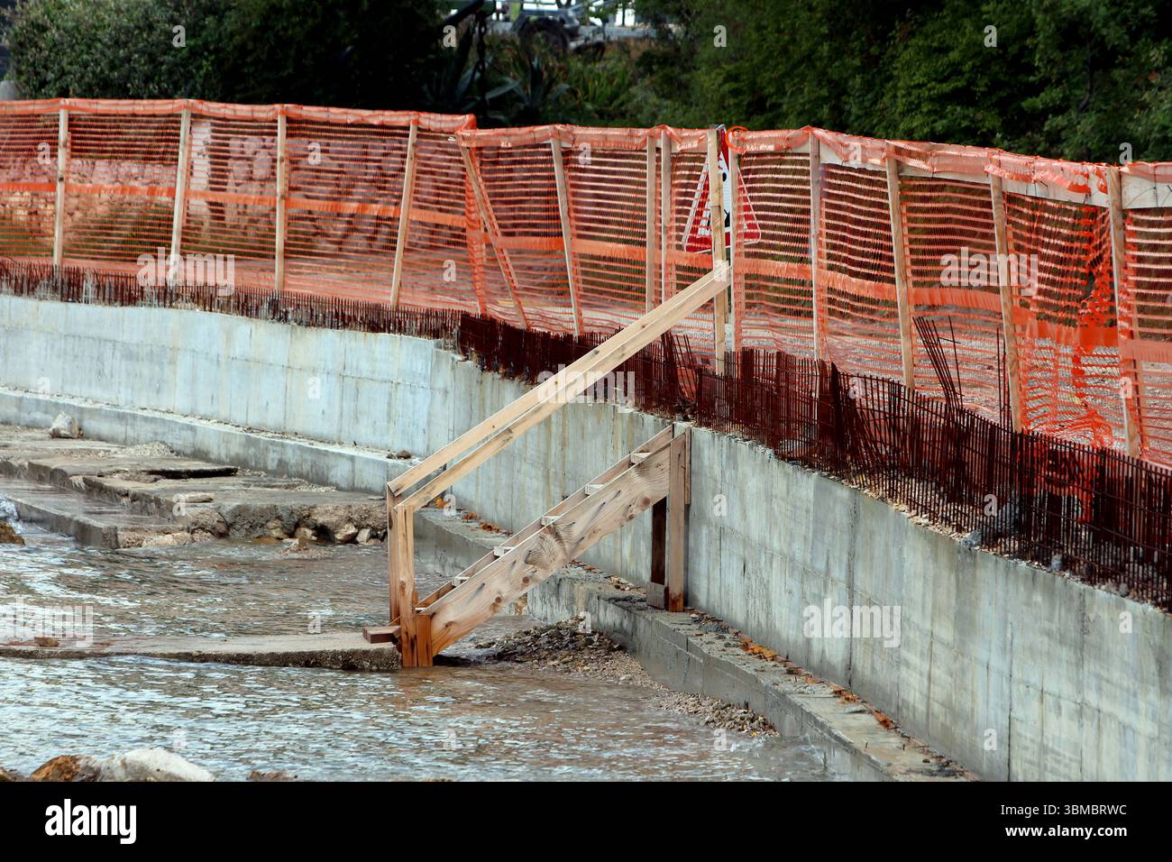 Concrete retaining wall topped with orange plastic safety fencing runs ...