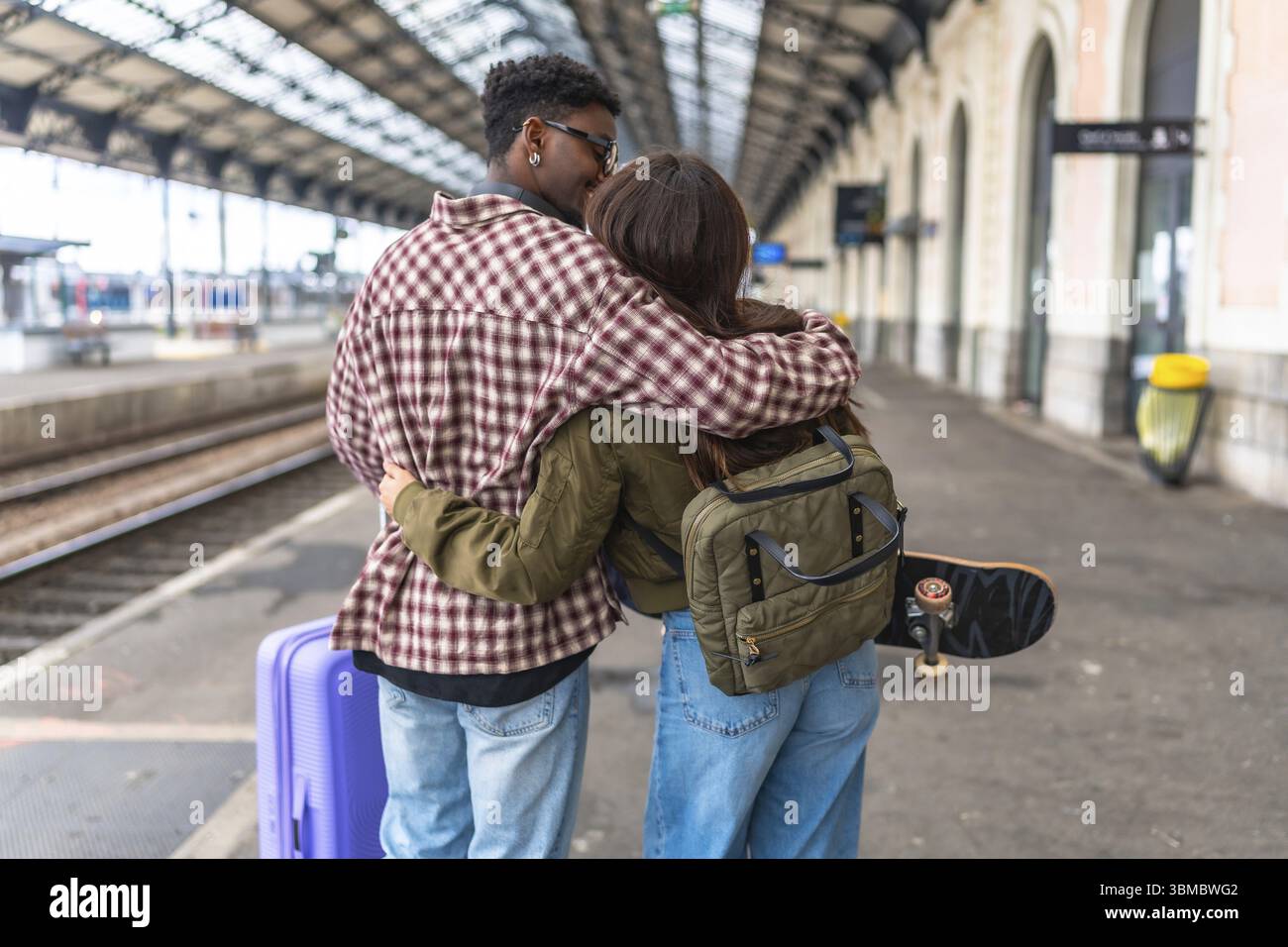 Young couple kissing and hugging on a train station platform, ready for their journey, with ...