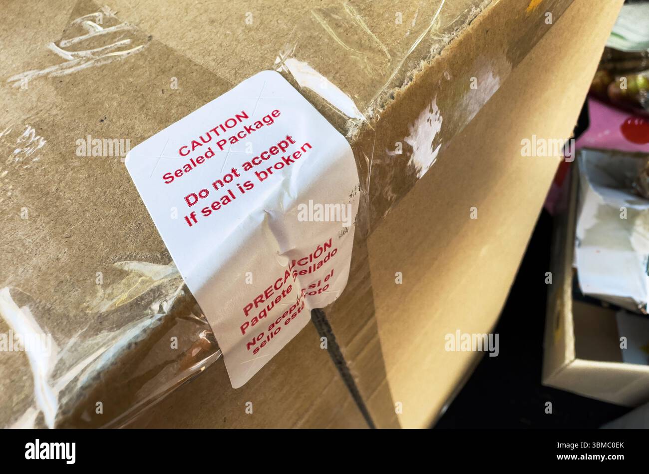 A close-up of a cardboard package corner shows a white caution sticker ...