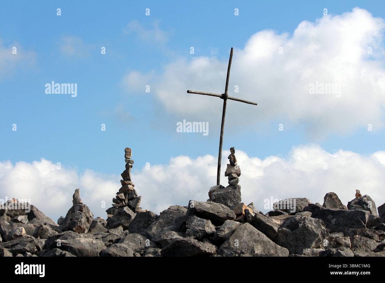 Simple wooden cross stands among balanced rock cairns on a rocky ...