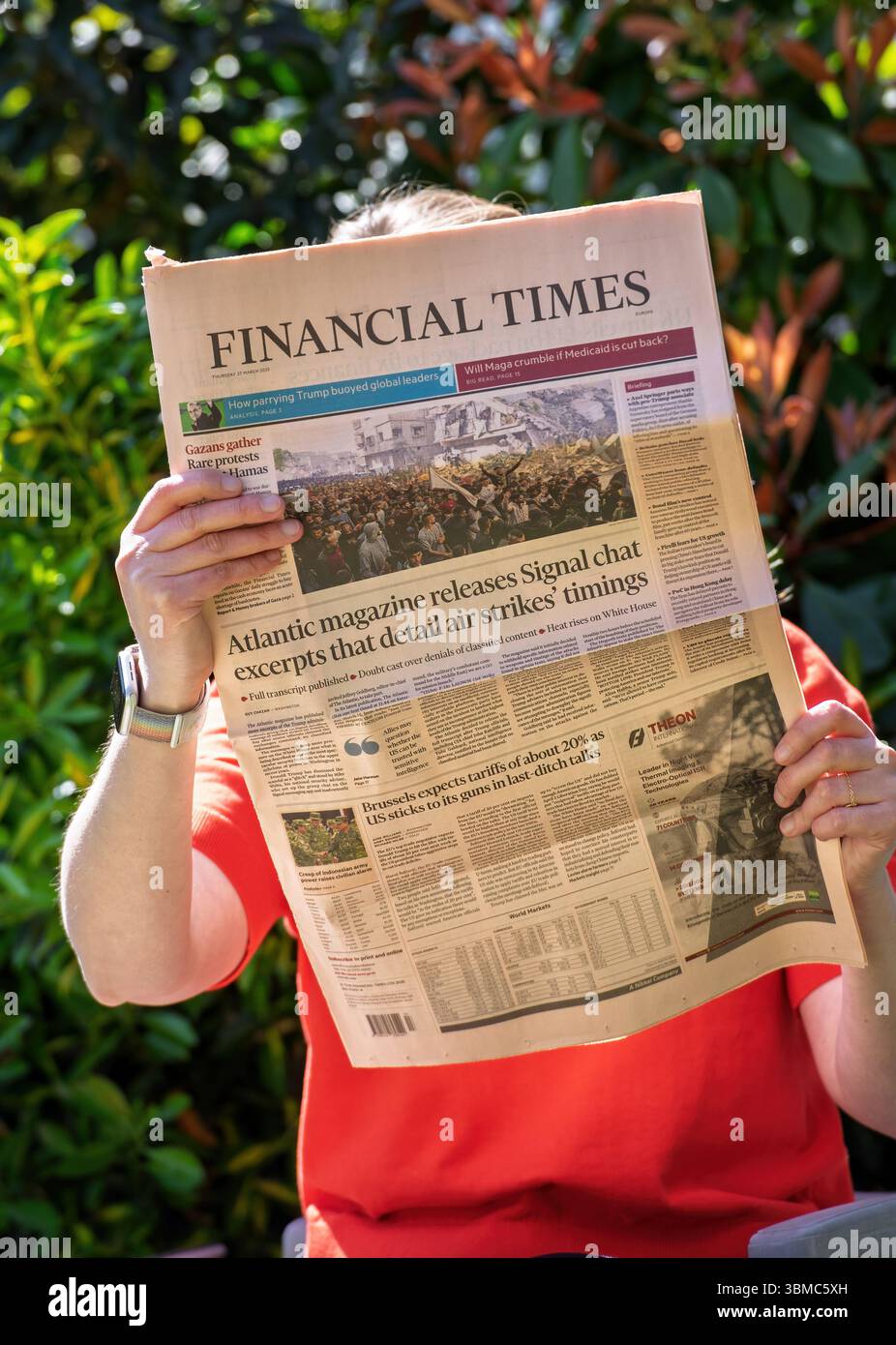 Person in red shirt reading Financial Times newspaper outdoors with ...