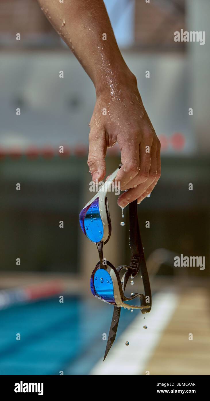 Hand holding wet swimming goggles poolside with water droplets dripping ...