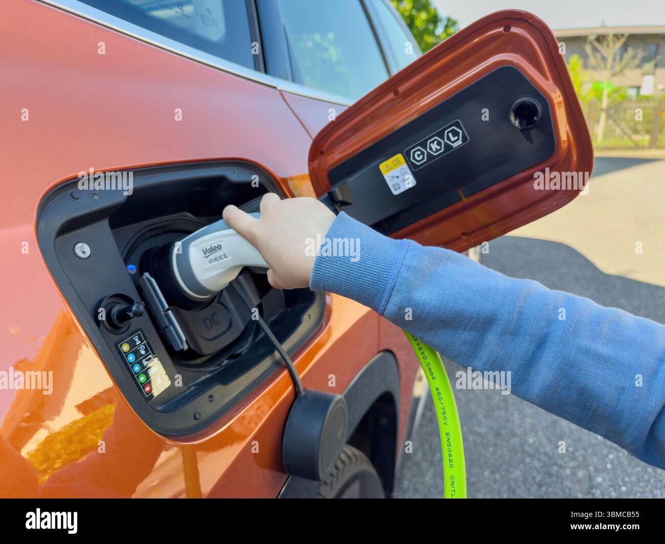 Paris, France - Apr 30, 2025: Child's hand connects Valeo Ineez charger to orange electric ...