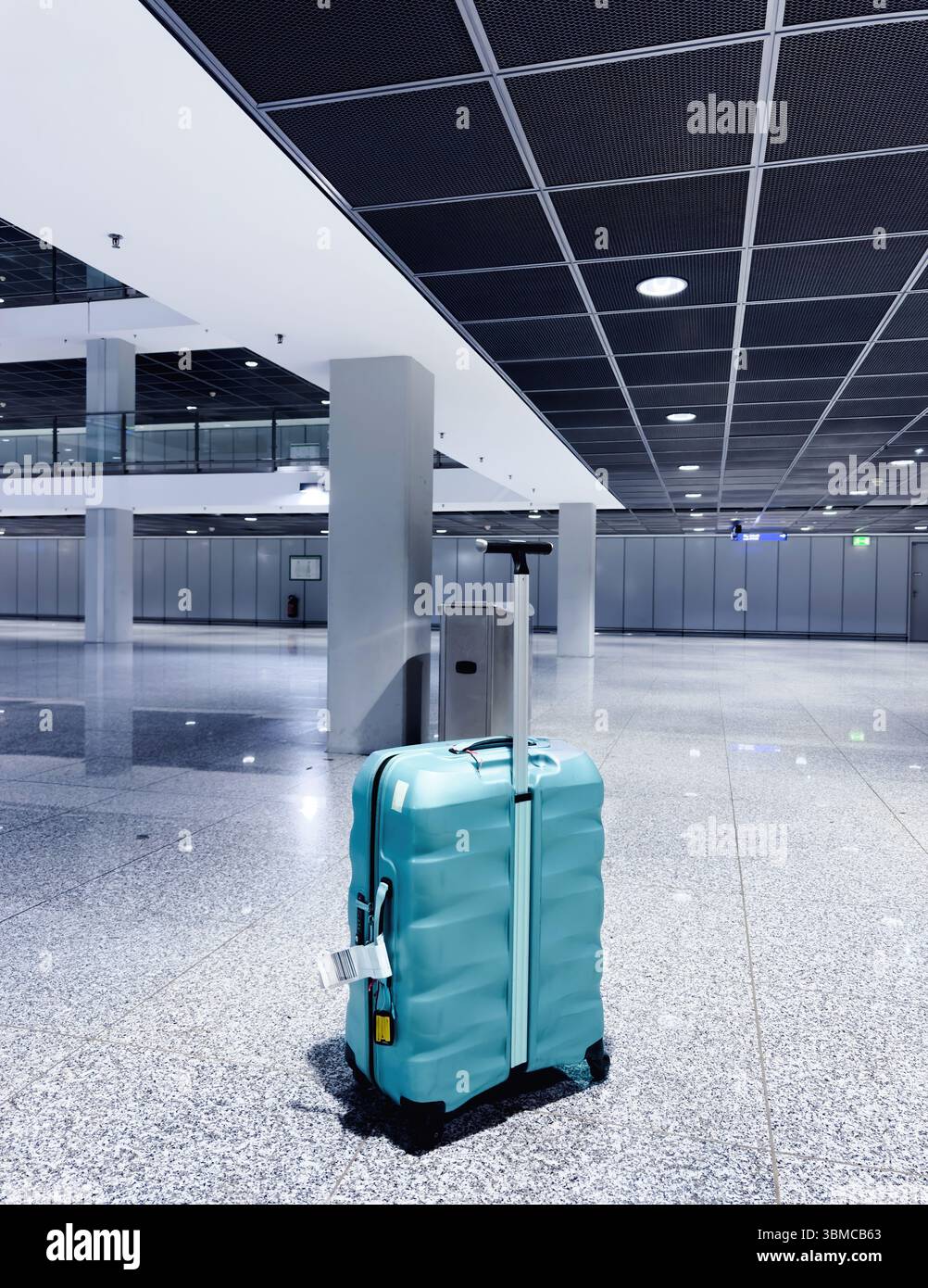 A turquoise hard-shell suitcase stands upright on the polished floor of ...