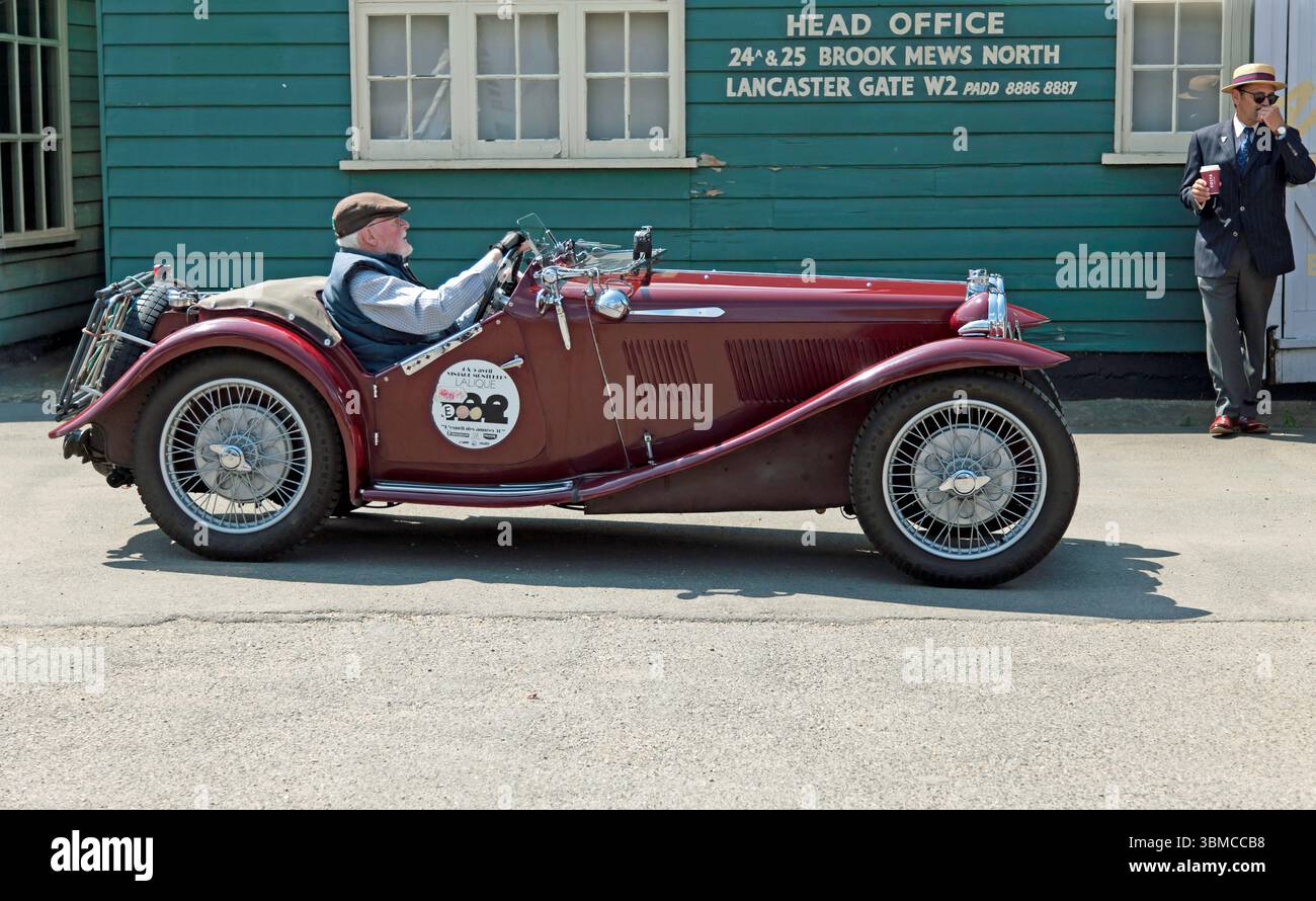 A Red 1933, MG L2 Magna, Passes in front of some original workshops at the Brooklands Museum ...