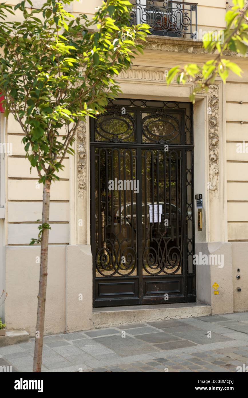A photograph of an ornate black iron gate entrance to a Parisian building. The gate features ...