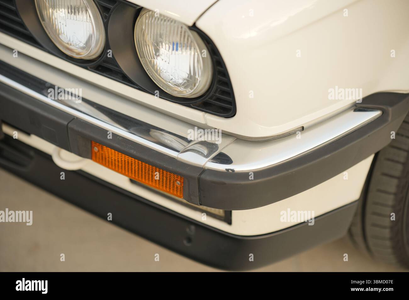 A detailed closeup of a classic vintage BMW e30 white cars front end showcasing chrome detailing ...