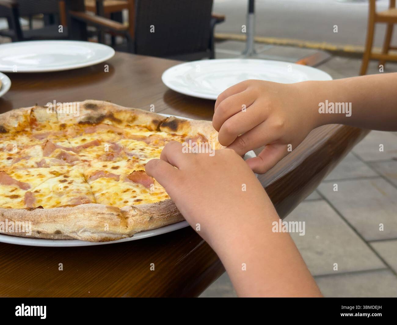 View of children's hands tearing one piece from a whole pizza in a ...