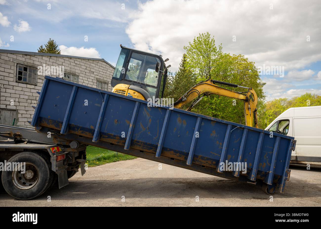 Blue industrial truck carrying a yellow mini excavator in its container ...