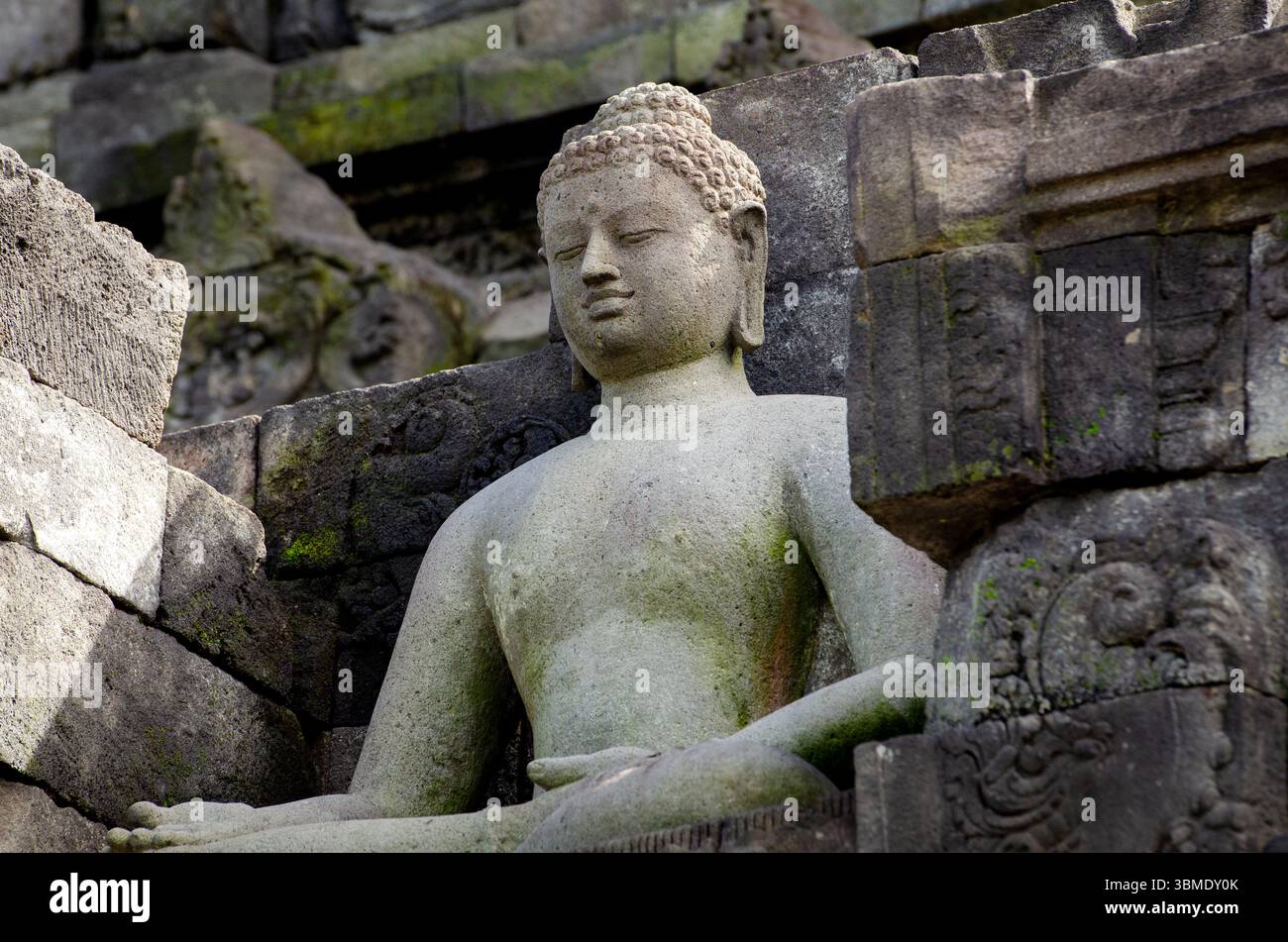 Ancient Buddha statue seated among stone ruins at Borobudur Temple, a ...