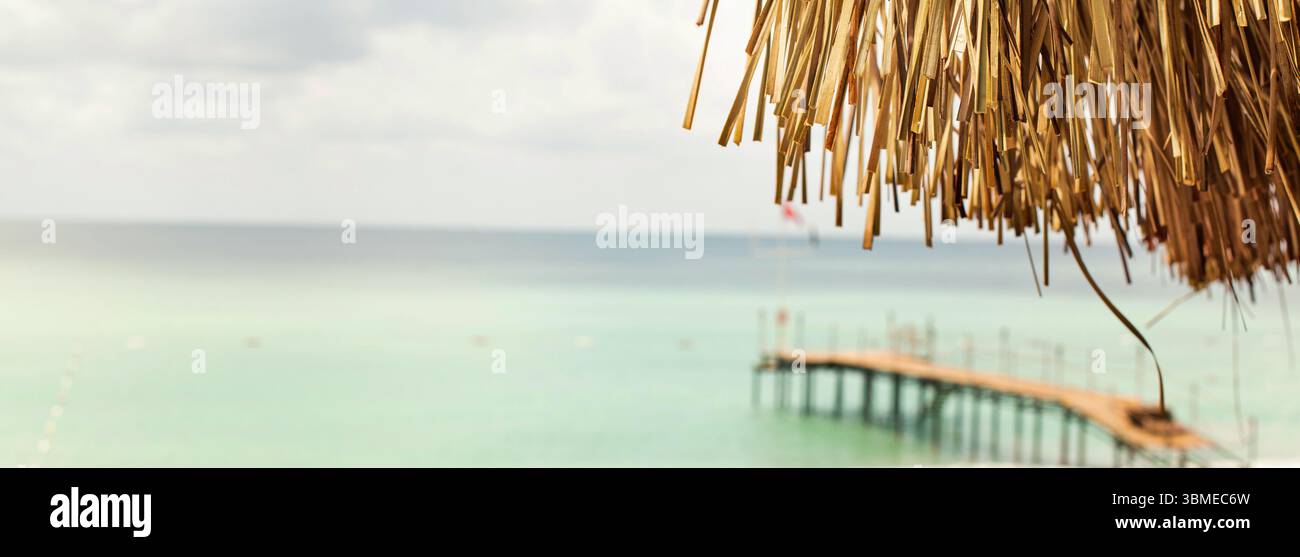 Thatched roof with beautiful tropical beach with sand and wooden pier ...
