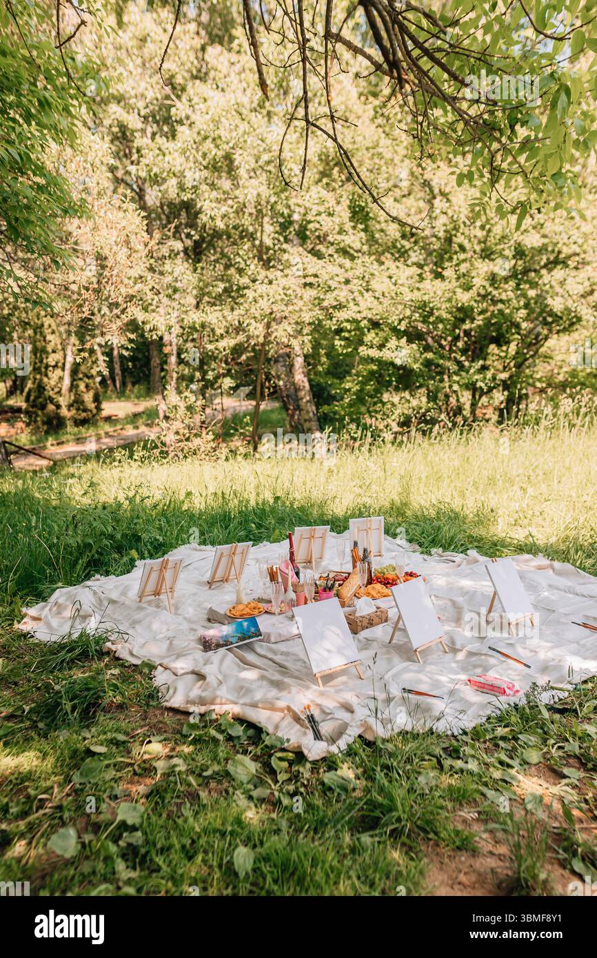 Outdoor art picnic setup with easels, blank canvases, and snacks arranged under tree shade Stock ...