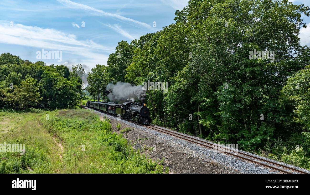 A vintage steam locomotive chugs down the railway tracks surrounded by ...