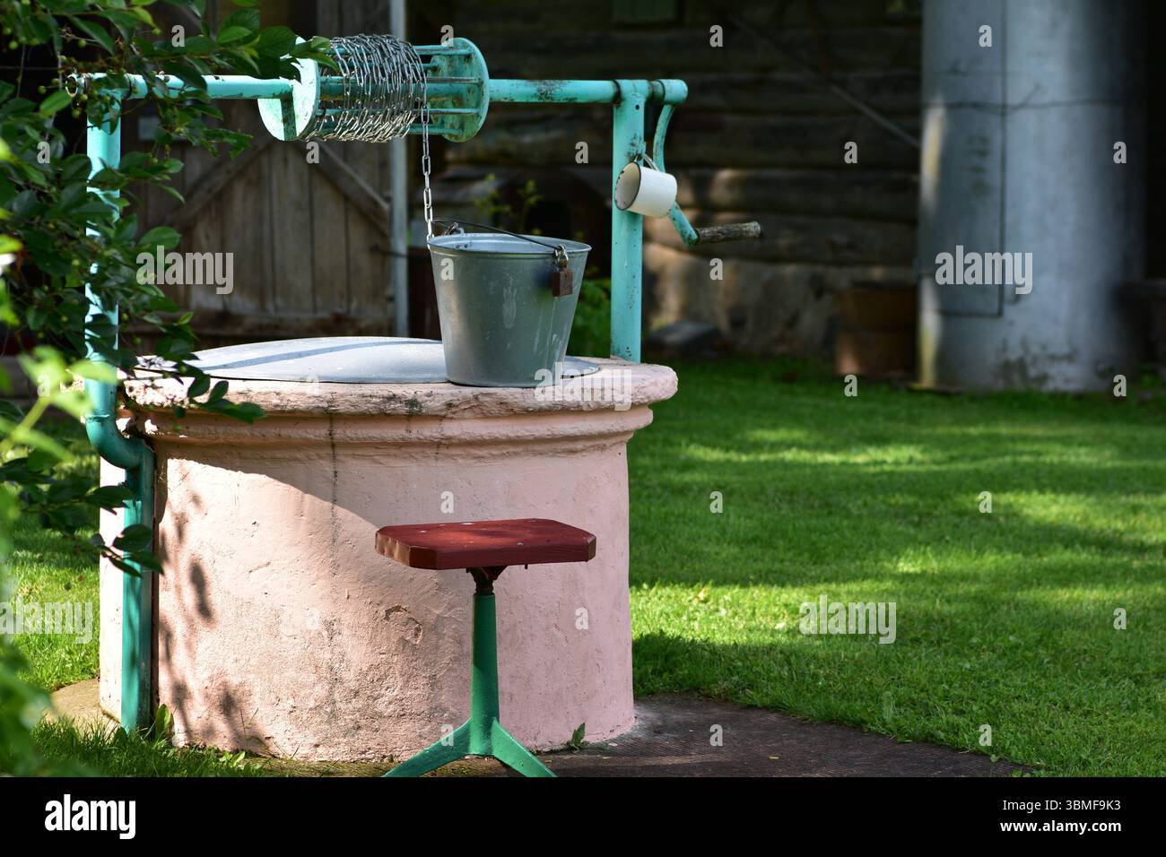 Old countryside water well with a green metal crank and a silver bucket ...