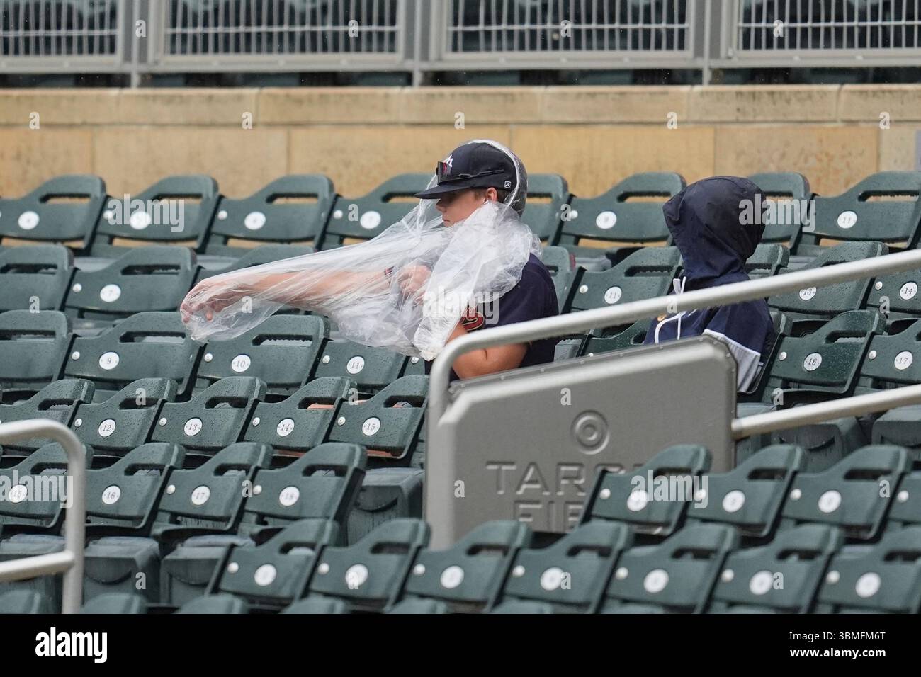 A fan puts on a rain cover during a rain delay before a baseball game ...
