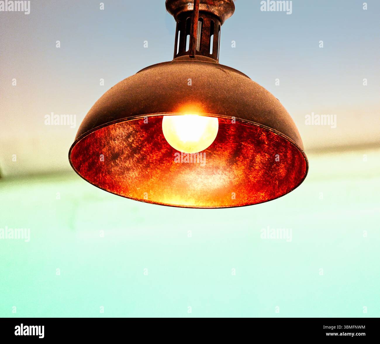 A warm light bulb glows inside a rustic metal lampshade, providing ...