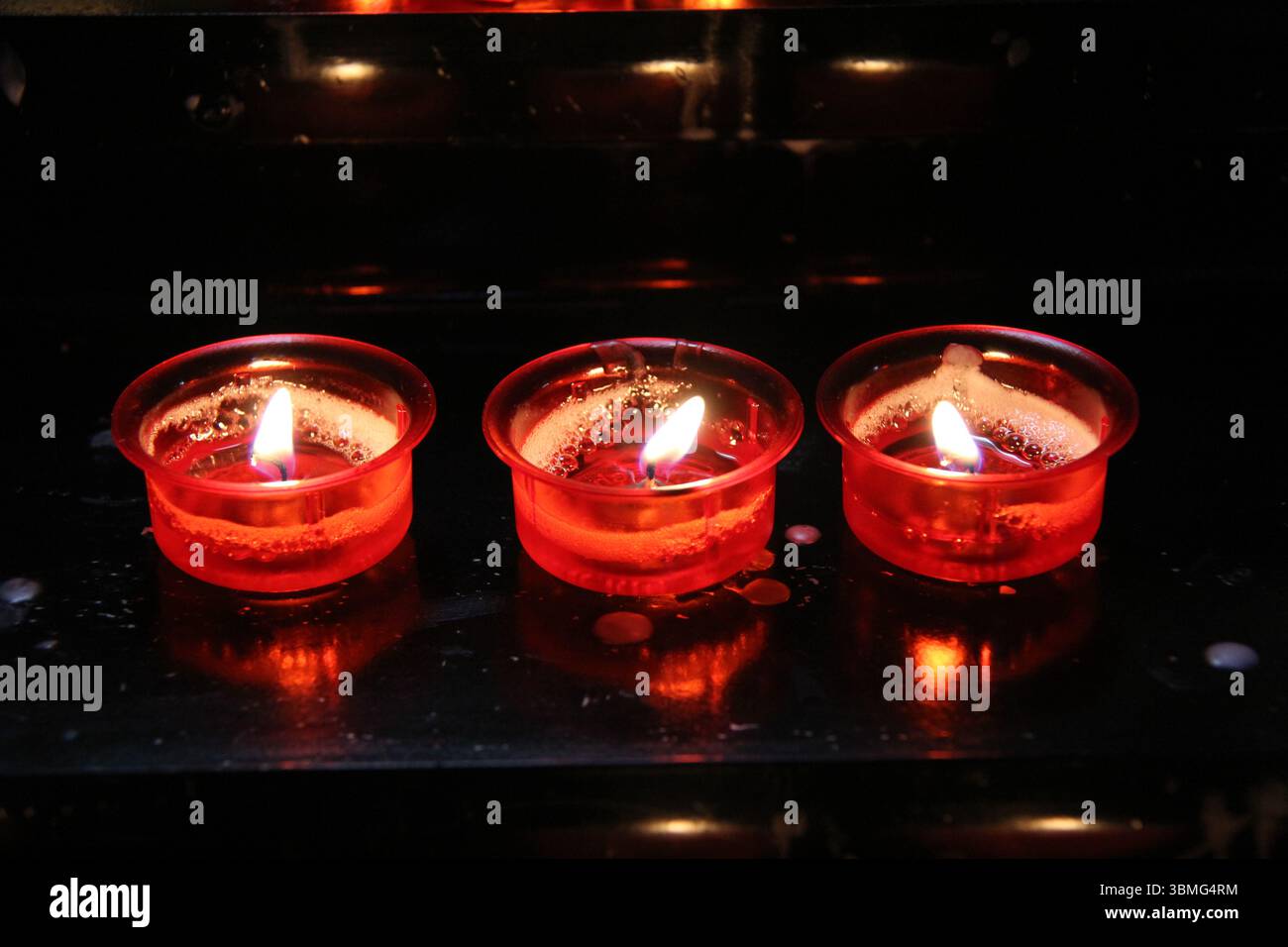 Three red memorial candles burning on a reflective black surface ...