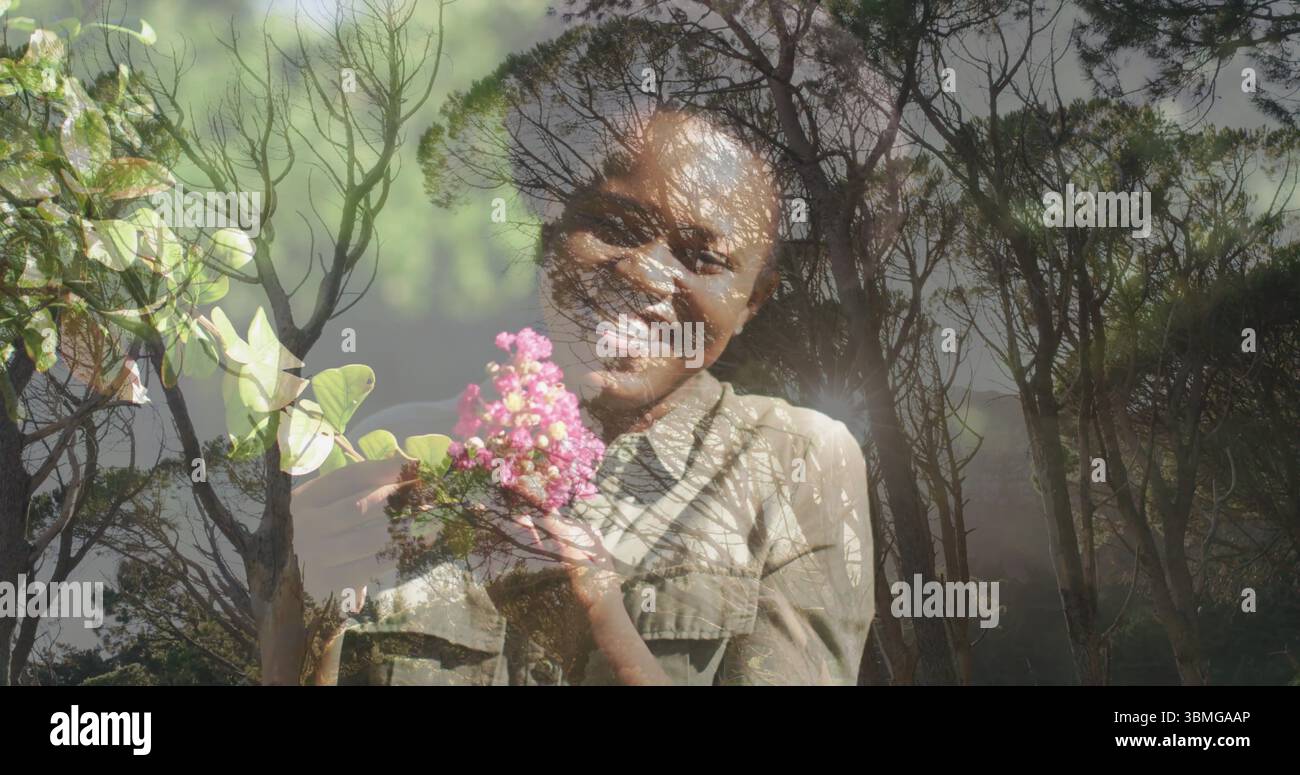Smiling mid adult woman holding pink flowers in woodland portrait, with ...