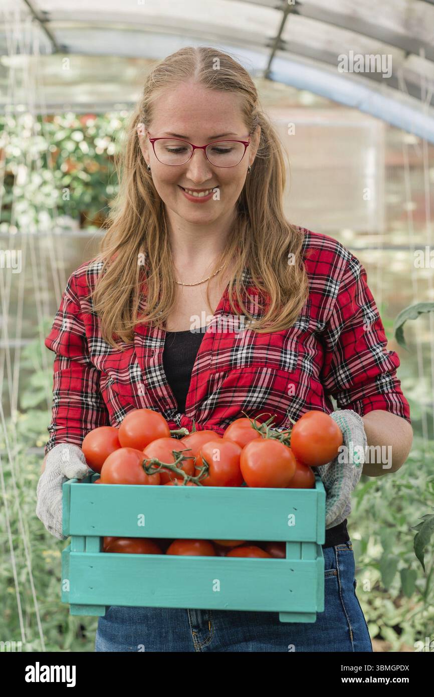 Organic female farmer holding box full of fresh produce on her farm ...