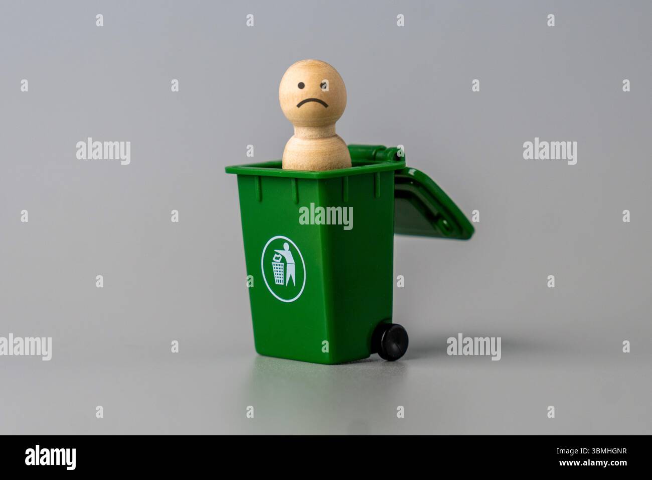 A small wooden figure with a sad face on it is placed inside a trash ...