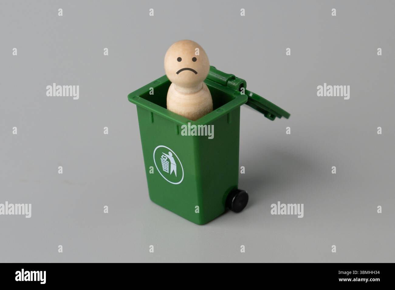 A small wooden figure with a sad face on it is placed inside a trash ...